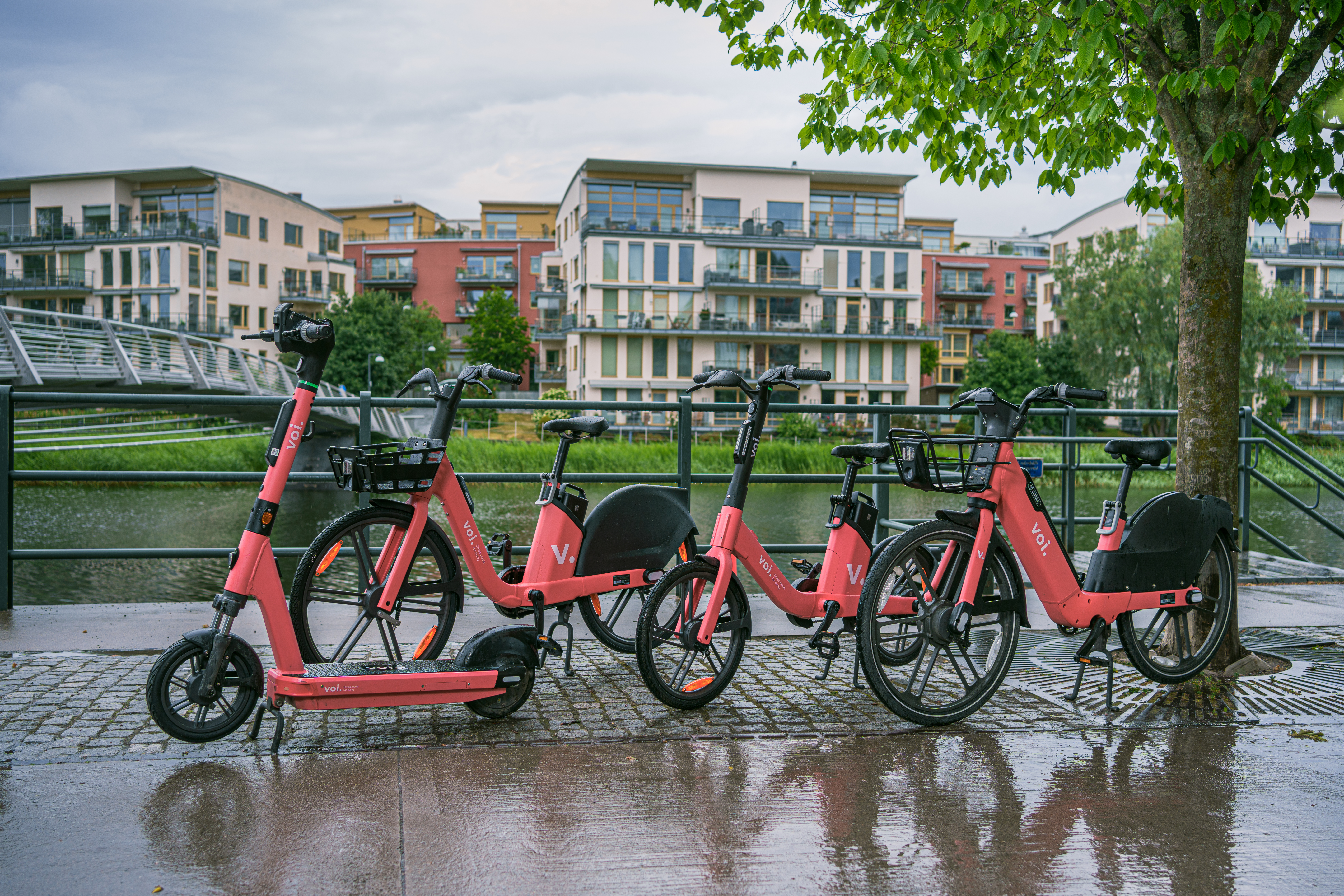 One red e-scooter and three red e-bikes are parked next to a canal in ...